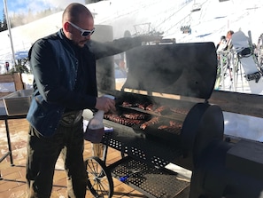 Pessoa grelhando carne ao ar livre com uma churrasqueira portátil com rodinhas.