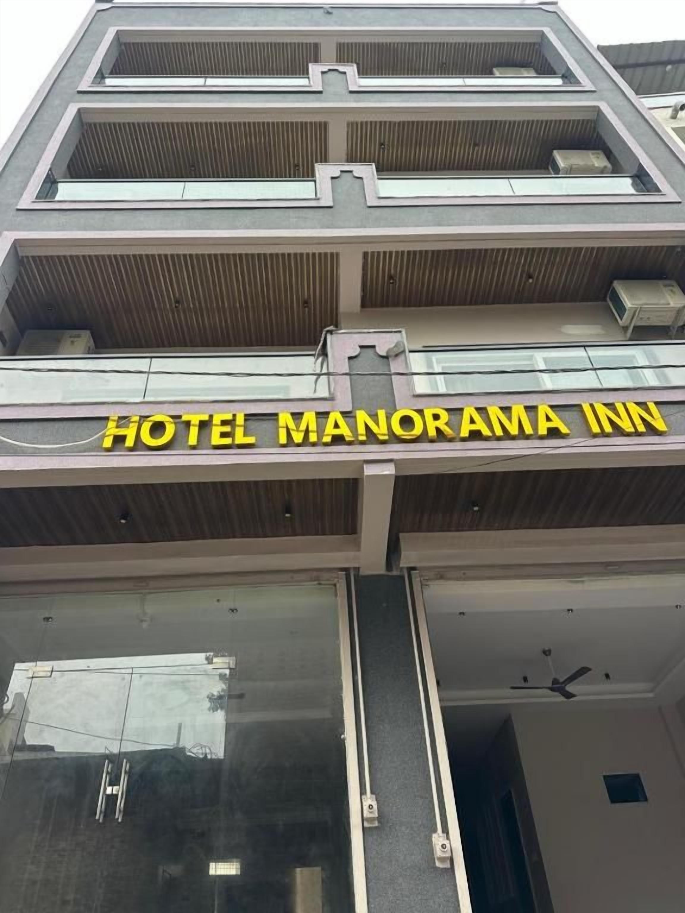 Um hotel com design moderno, apresentando uma placa chamativa para 'Hotel Manorama Inn' e entrada de vidro.
