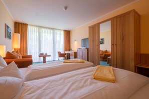 Quarto de hotel com duas camas, uma escrivaninha, uma cadeira, uma televisão e um guarda-roupa.