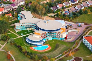 Um hotel moderno com vários edifícios curvos, uma piscina central e um gramado bem cuidado.