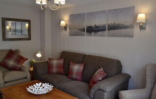 Sala de estar com sofá, duas poltronas, mesa de centro e luminárias fixadas na parede.
