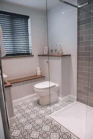 Casa de banho moderna com cabine de duche em vidro, sanita e um prateleira com artigos de higiene pessoal.
