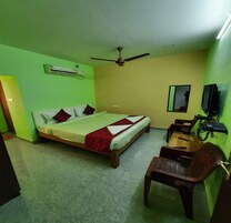 Quarto com cama, escrivaninha, cadeira, ar-condicionado, ventilador de teto e televisão.
