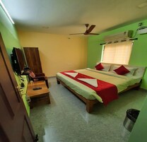 Quarto com cama, escrivaninha, cadeira, ventilador de teto, ar condicionado e janela com cortinas.