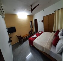 Quarto de hotel com cama, escrivaninha, cadeira, televisão e ventoinha no teto.