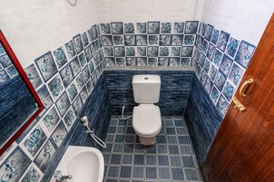 Casa de banho com sanita, bidé e lavatório. As paredes estão revestidas com um padrão azul e branco.