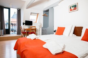 Quarto de hotel com uma cama grande, uma escrivaninha com computador e vista para um edifício.