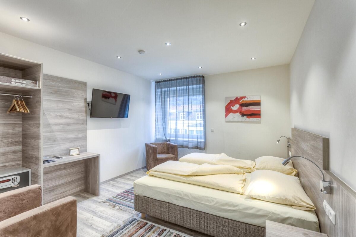 Quarto moderno com cama, escrivaninha, cadeira e TV fixada na parede.