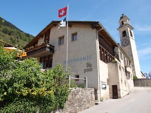 Um edifício com uma placa indicando 'Ristorante Stia Granda', uma varanda, uma torre do relógio e uma bandeira.