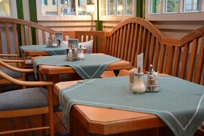 Interior de restaurante com cadeiras e mesas de madeira, cada uma com toalha de mesa verde e acessórios.