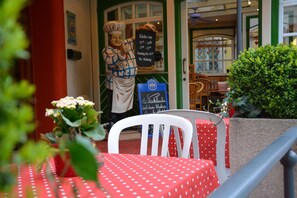 Entrada de restaurante com estátua de chef, cardápio em lousa e toalha de mesa com bolinhas.
