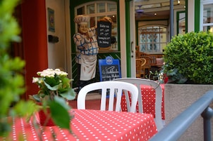 Entrada de restaurante com estátua de chef, cardápio em lousa e toalha de mesa com bolinhas.