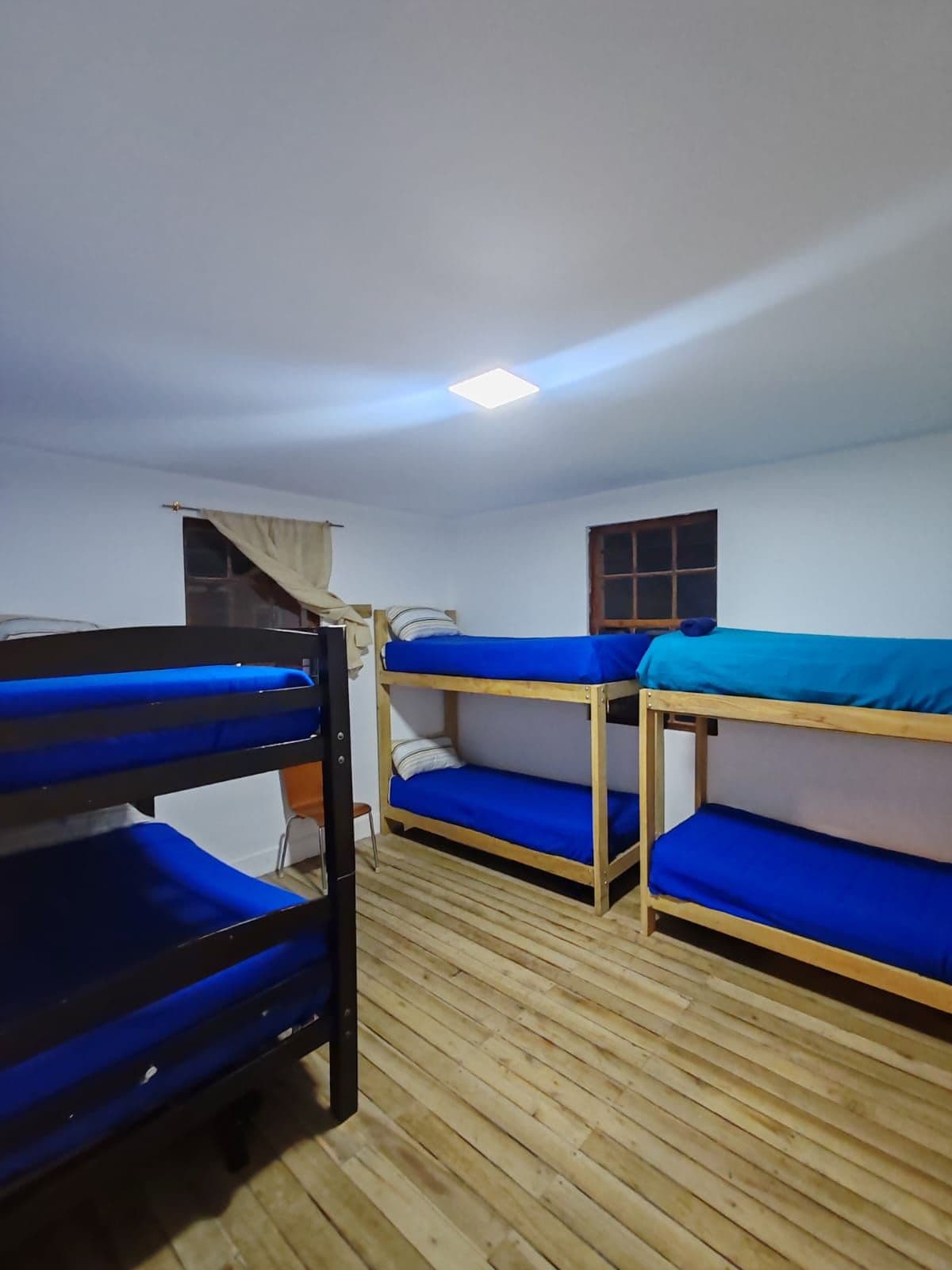 Quarto em dormitório com beliches, janela e luminária no teto.