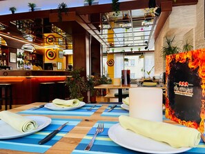 Um restaurante com área de bar, mesas preparadas para refeições e uma parede decorativa com tema de fogo.