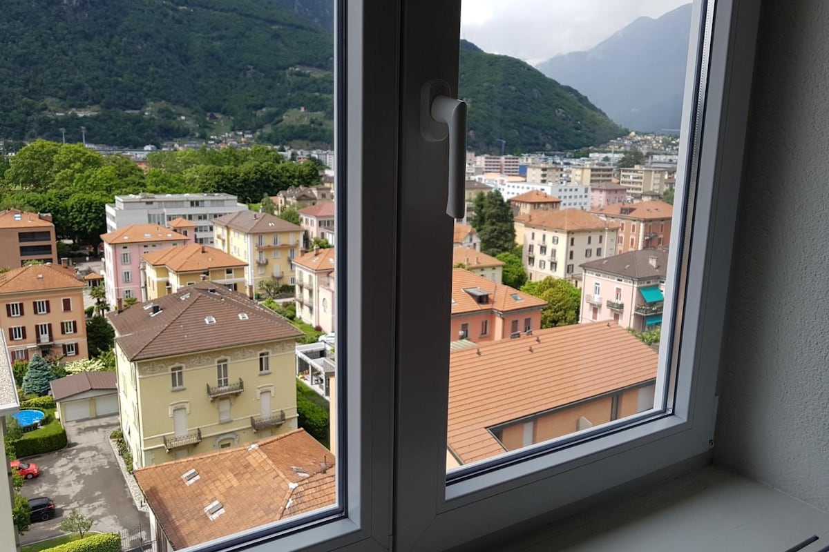 Janela com vista para área residencial, incluindo edifícios e uma montanha ao fundo.