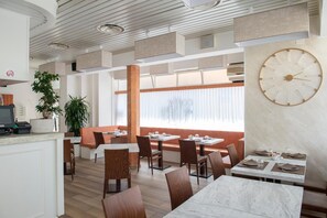 Interior moderno de restaurante com piso de madeira, paredes brancas e um relógio de parede grande.