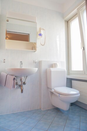 Casa de banho com lavatório branco, sanita e janela que proporciona luz natural.