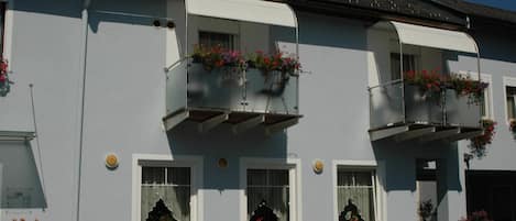 Um edifício com várias janelas, algumas adornadas com caixas de flores, e uma varanda com guarda-corpo.