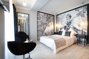 Quarto com uma cama grande, uma cadeira, uma mesinha de cabeceira e uma parede com um mural detalhado.