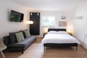 Quarto com cama, sofá, televisão, janela e abajures.