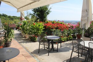 Um pátio externo com mesas e cadeiras, rodeado por vasos de plantas e flores.