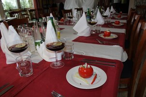 Mesa de restaurante posta com taças de vinho, uma garrafa e um prato com tomate.
