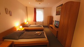 Quarto de hotel com duas camas, televisão, guarda-roupa e janela com cortinas.