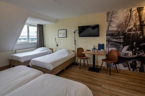 Quarto de hotel com duas camas de solteiro, uma escrivaninha com cadeira, televisão de tela plana e uma janela grande.