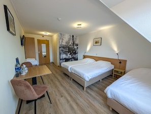 Quarto de hotel com cama, escrivaninha, cadeira e luminária na parede.