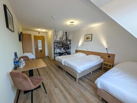 Quarto de hotel com cama, escrivaninha, cadeira e luminária na parede.