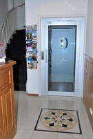 Um corredor com piso de azulejos, uma porta com puxador e uma escada ao fundo.