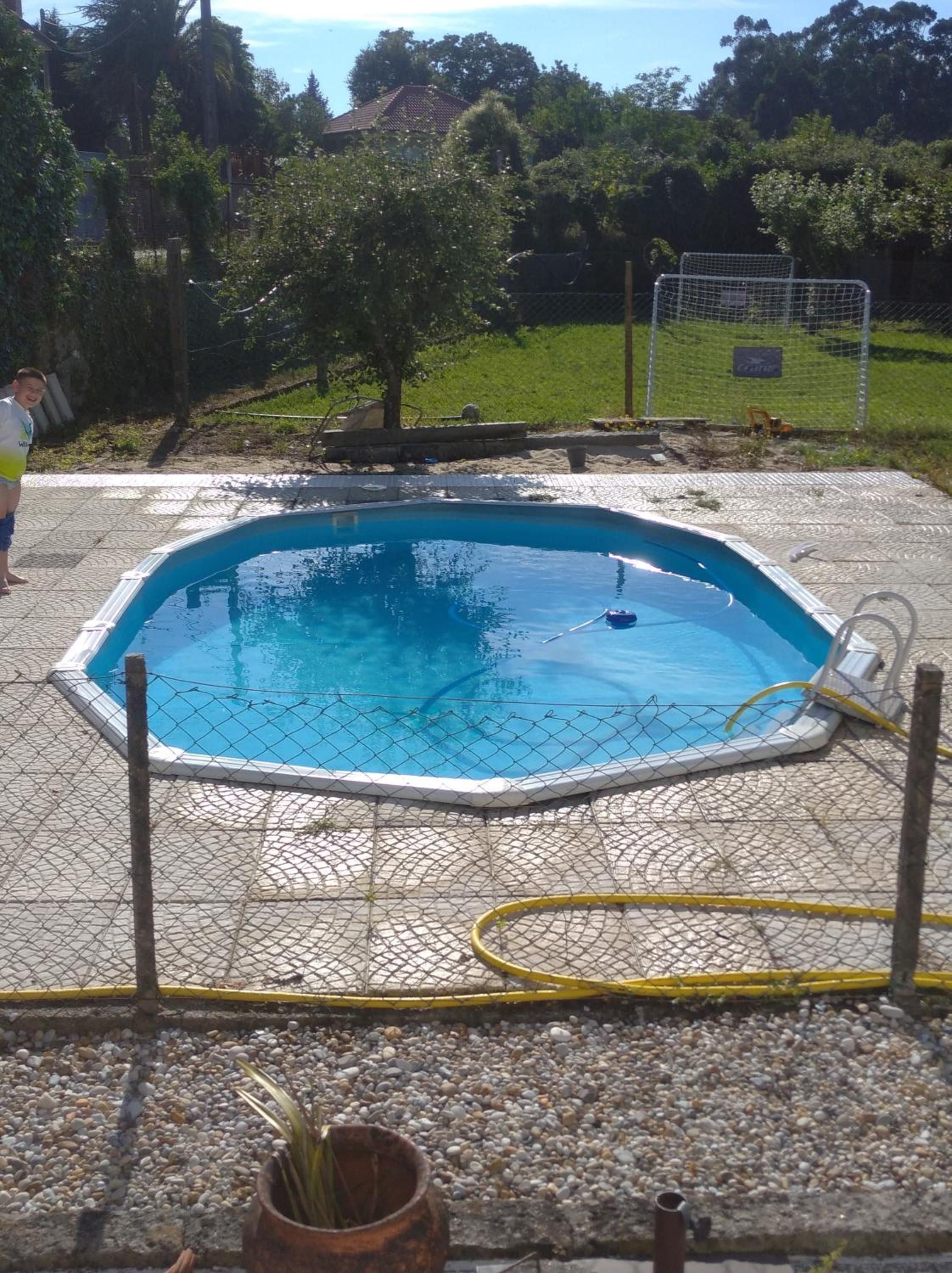 Uma piscina cercada por uma grade, uma mangueira e um vaso de planta.