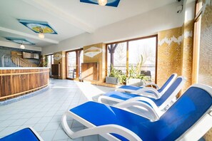 Área interna de piscina com luz solar, cadeiras de descanso, balcão de recepção e vista para o exterior.