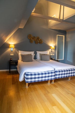 Quarto com teto inclinado, duas camas com roupa de cama xadrez, luminárias fixadas na parede e um objeto decorativo na parede.