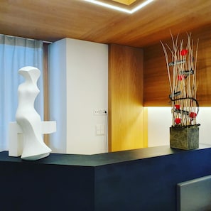Um balcão de recepção moderno com design minimalista, uma escultura abstrata branca e uma arrumação decorativa de plantas.