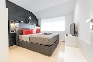Quarto moderno com cama, televisão e janela.
