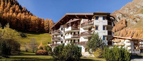 Um hotel com várias andares e varandas, rodeado por uma paisagem montanhosa e folhagem outonal.