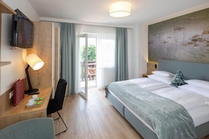 Quarto de hotel com cama, escrivaninha, cadeira, televisão e um quadro na parede.