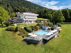 Um hotel com vários andares, piscina, área de estar externa e vista para uma encosta arborizada.