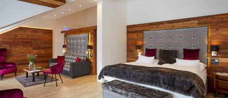 Quarto moderno com cama grande, área de estar com sofá e cadeiras, e teto de madeira.