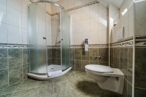 Casa de banho com cabine de duche em vidro, sanita e paredes em azulejo.