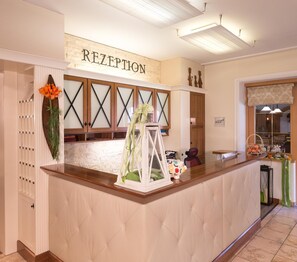 Uma área de recepção com uma placa indicando 'RECEPTION', um balcão de madeira, um mural de avisos e uma planta decorativa.