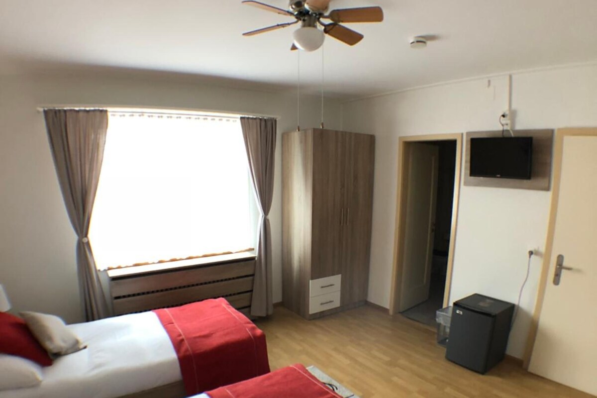 Quarto de hotel com duas camas, ventoinha no teto, televisão e guarda-roupa.