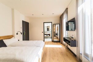 Quarto de hotel com cama, mesa de cabeceira, espelho e televisão fixada na parede.