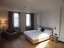 Quarto moderno com cama de madeira, mesa de cabeceira, abajur e uma cadeira.