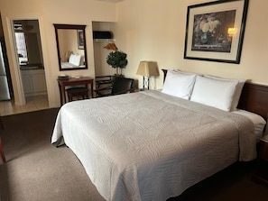 Quarto de hotel com uma cama grande, uma escrivaninha, uma cadeira, um abajur, um espelho e um quadro na parede.