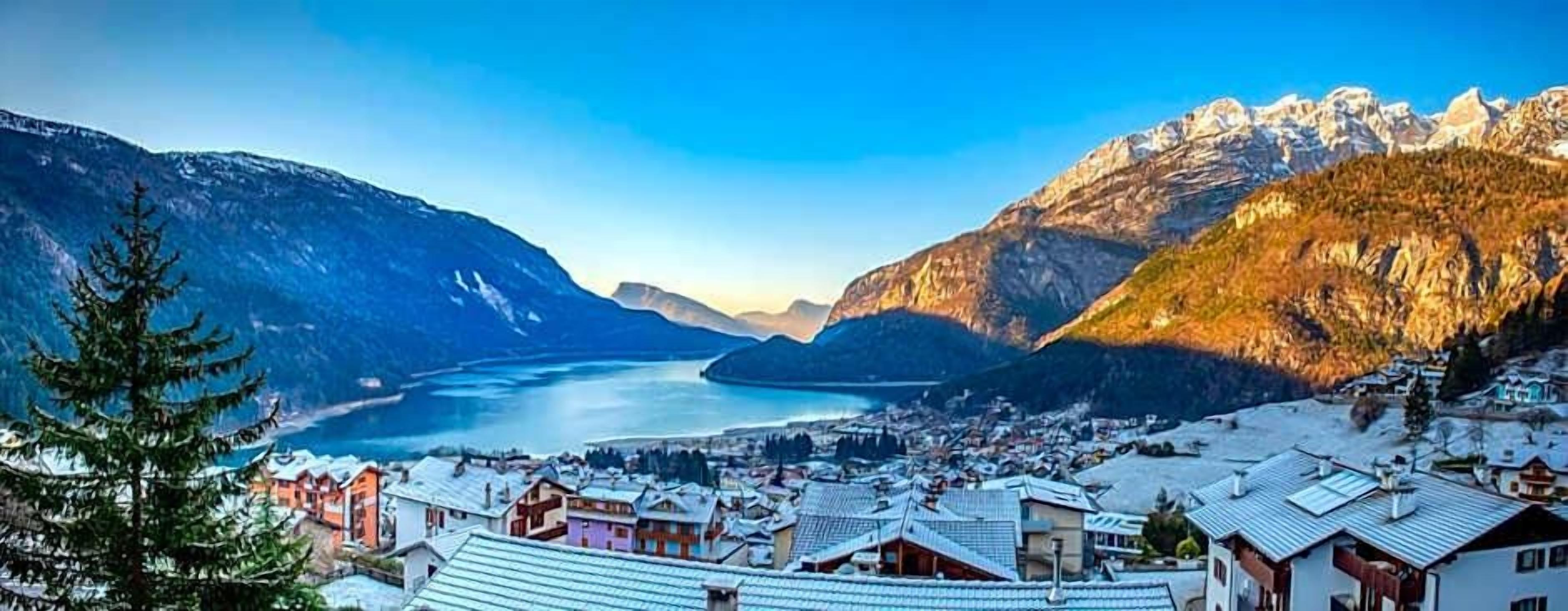 Paisagem montanhosa com um lago, edifícios cobertos de neve e céu limpo.