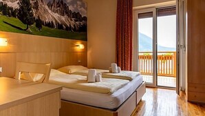Quarto de hotel com cama, escrivaninha e vista para uma varanda com grade de madeira.