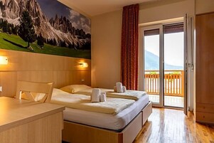Quarto de hotel com cama, escrivaninha e vista para uma varanda com grade de madeira.