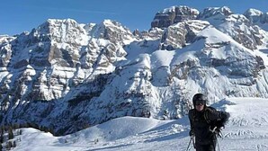 Uma pessoa esquiando em uma encosta nevada, com montanhas ao fundo.